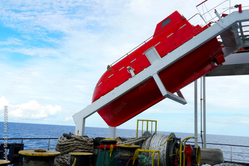 Orange free fall lifeboat secured on white launching ramp and ready to ...