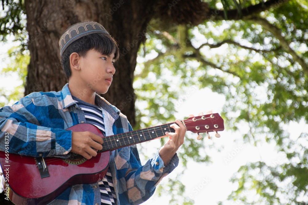 Asian cute muslim or islamic boy plays ukulele or acoustic guitar under ...