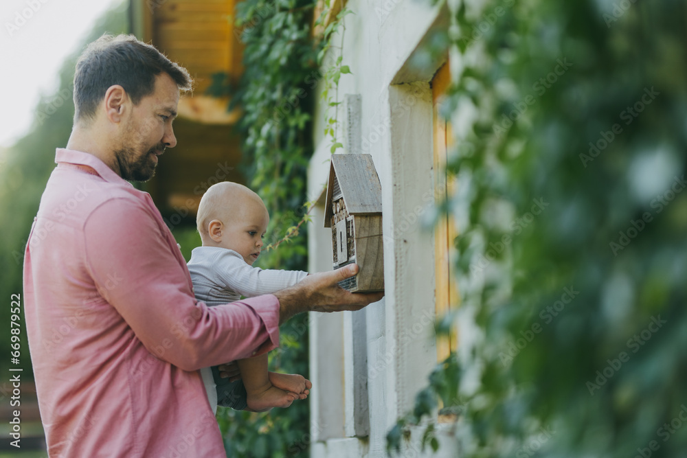 Father showing his baby son wooden insect house outdoors in the garden ...
