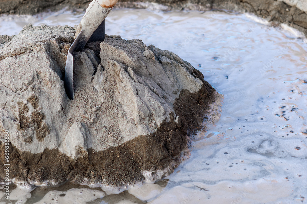 A mixture of cement and sand is soaked in water to mix the concrete by ...