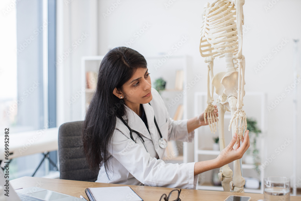 Competent female physician examining hands bones on plastic skeleton ...