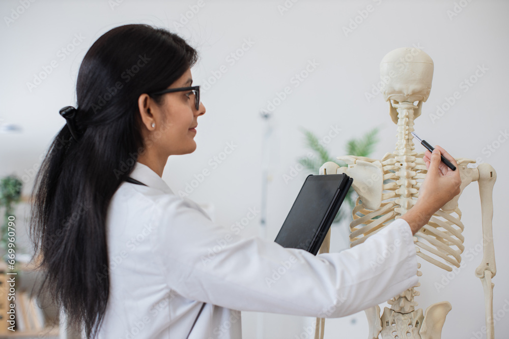 Side view of hindu medical worker with tablet pointing at spine while ...