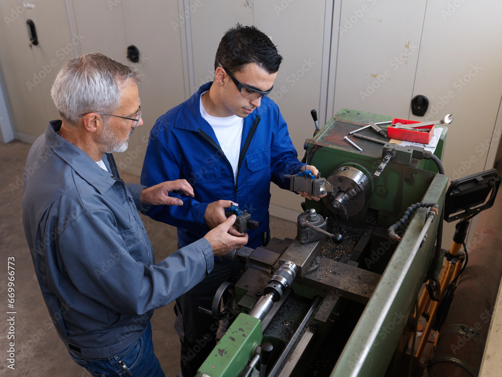 Instructor guiding apprentice using lathe machine at workshop Stock ...