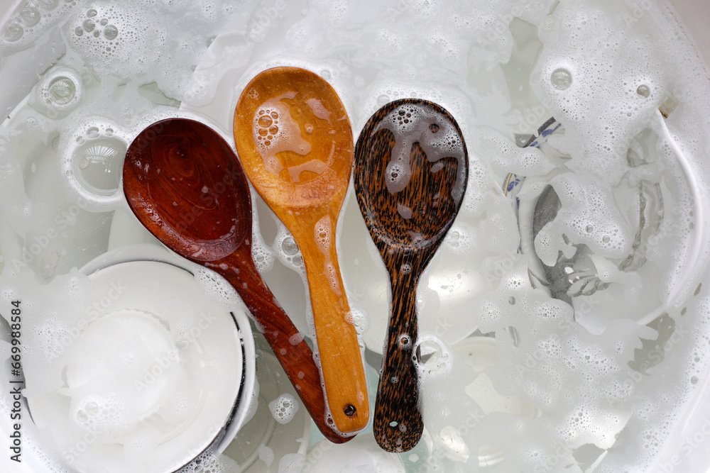 Wooden spoon and dishes in water and bubbles of dishwashing liquid ...