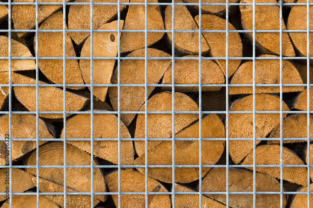 Wooden firewood logs are stacked behind a metal mesh. Wood texture and ...