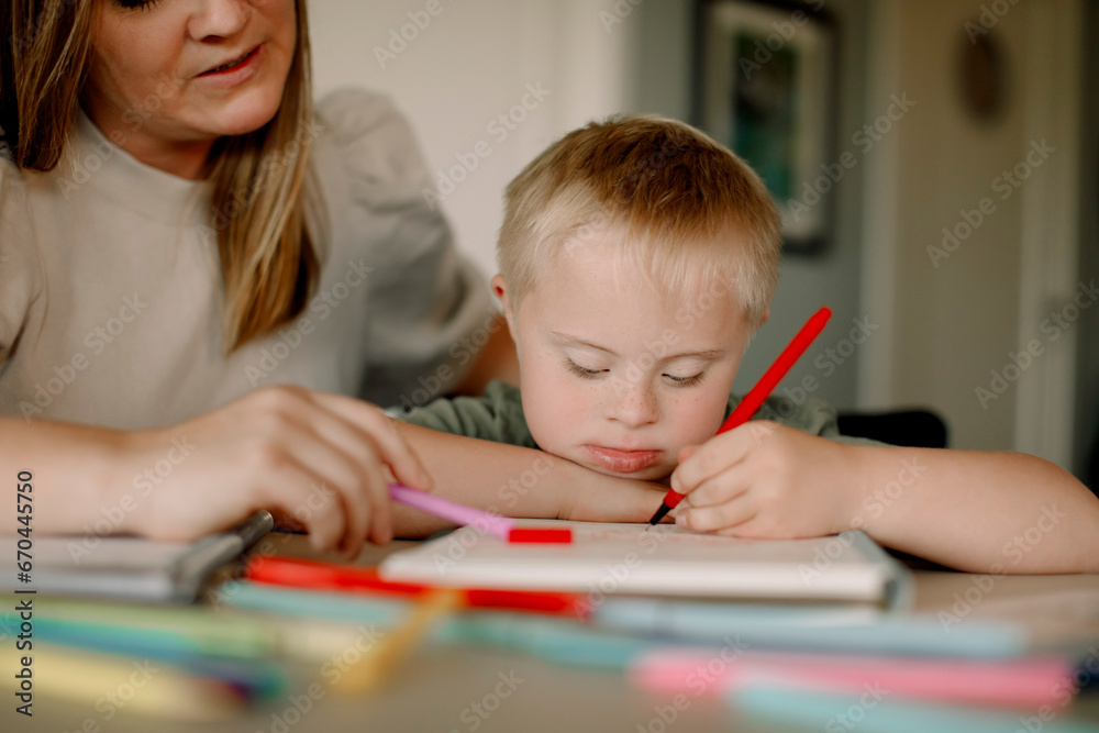 Boy with down syndrome drawing in book by mother at home Stock Photo ...