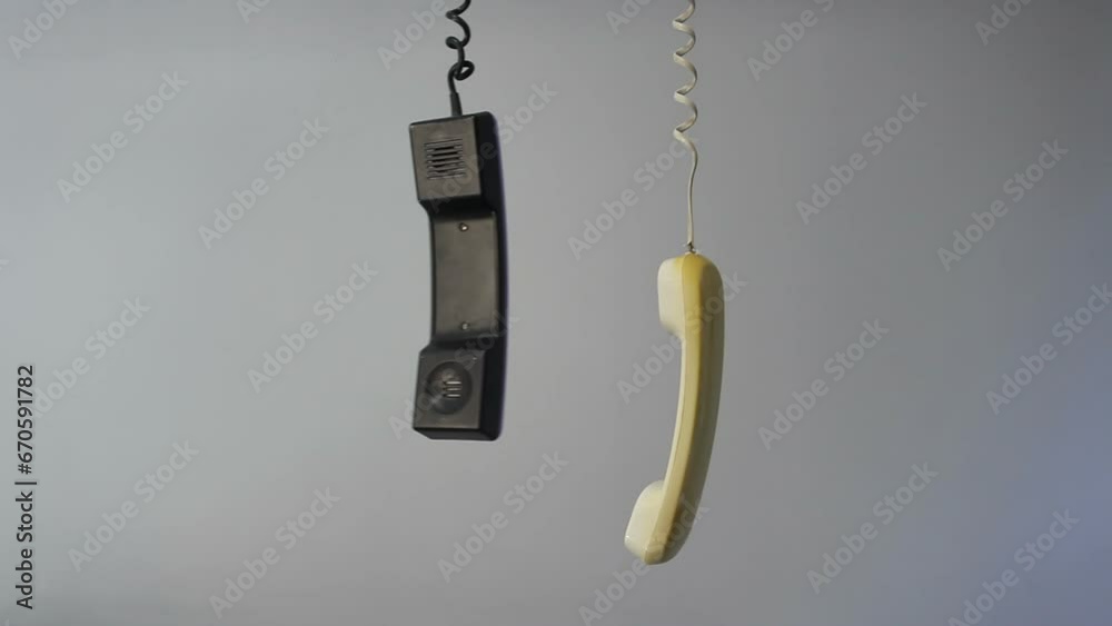 Two telephone handsets for landline phones hang on wires, on a gray ...