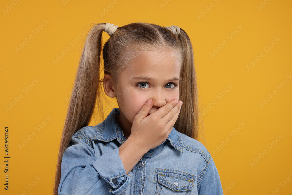 Embarrassed little girl covering her mouth with hand on orange ...