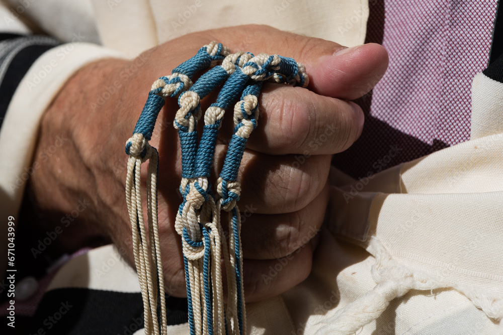 An Orthodox, Jewish man holds blue techelet tzitzit strings while ...
