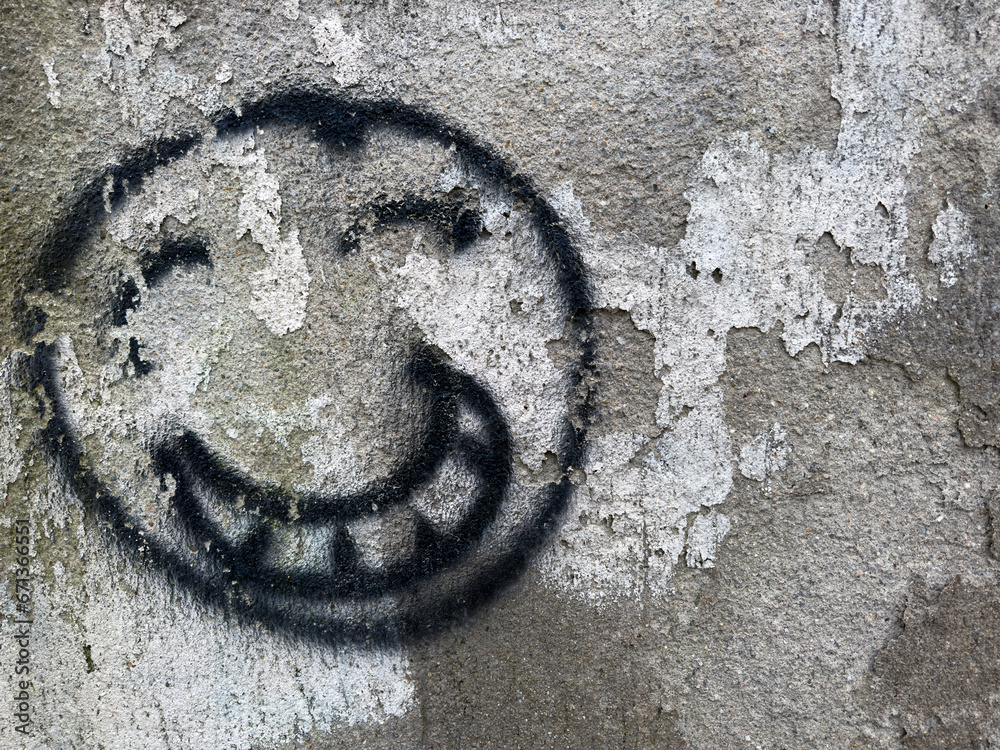 Emoji graffiti grinning on the crumbling plaster of a ruined wall ...