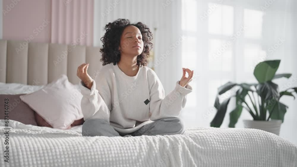 Smiling African american curly woman meditating sitting in bed at home ...