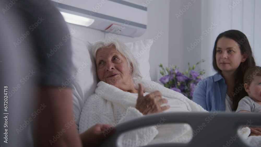 Female old patient lies in bed in bright hospital ward, spends time ...