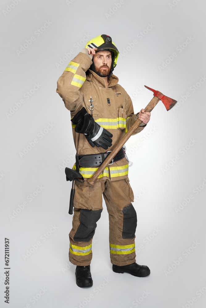 Concerned bearded firefighter in full gear holding red axe for fire ...