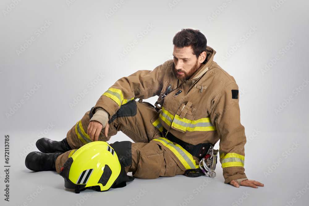 Tired male firefighter taking breath, while sitting on floor. Side view ...