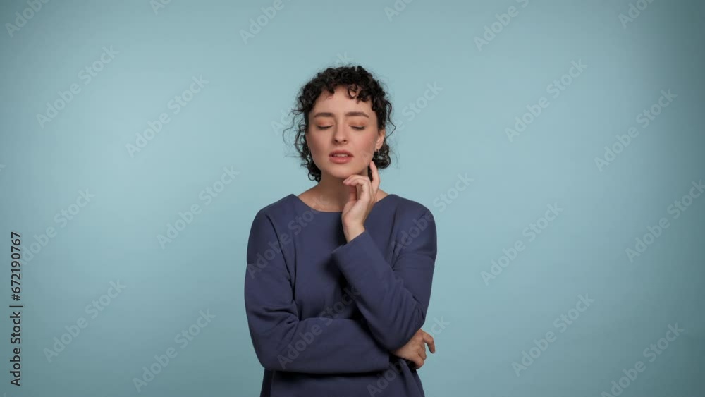Pensive young curly woman in blue sweater posing looking around ...