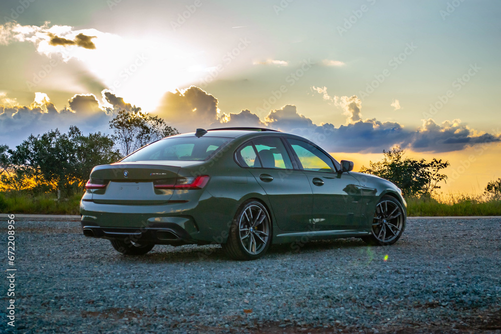 Rear end three quarters view of a military green BMW M340i, sunset sky ...