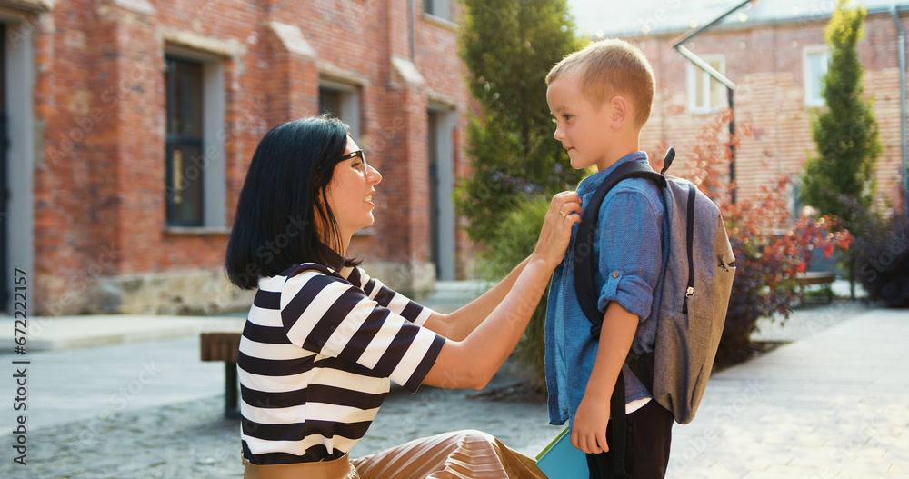 Caring mother helps her little school son and correct collar on shirt ...