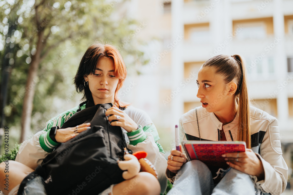 Two casually dressed high school girls study outdoors, discussing ...