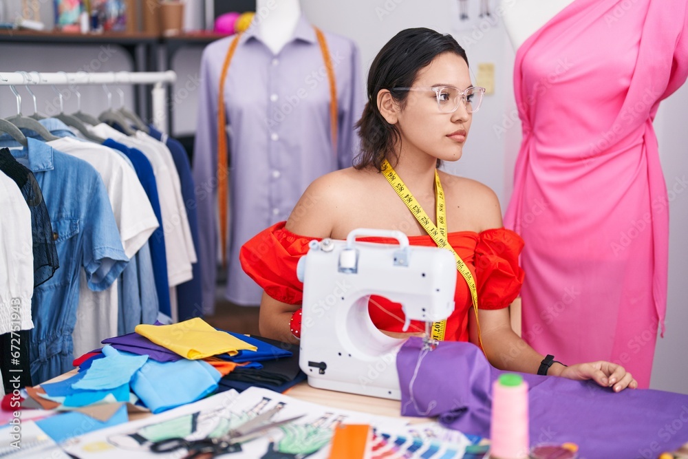 Hispanic young woman dressmaker designer using sewing machine looking ...