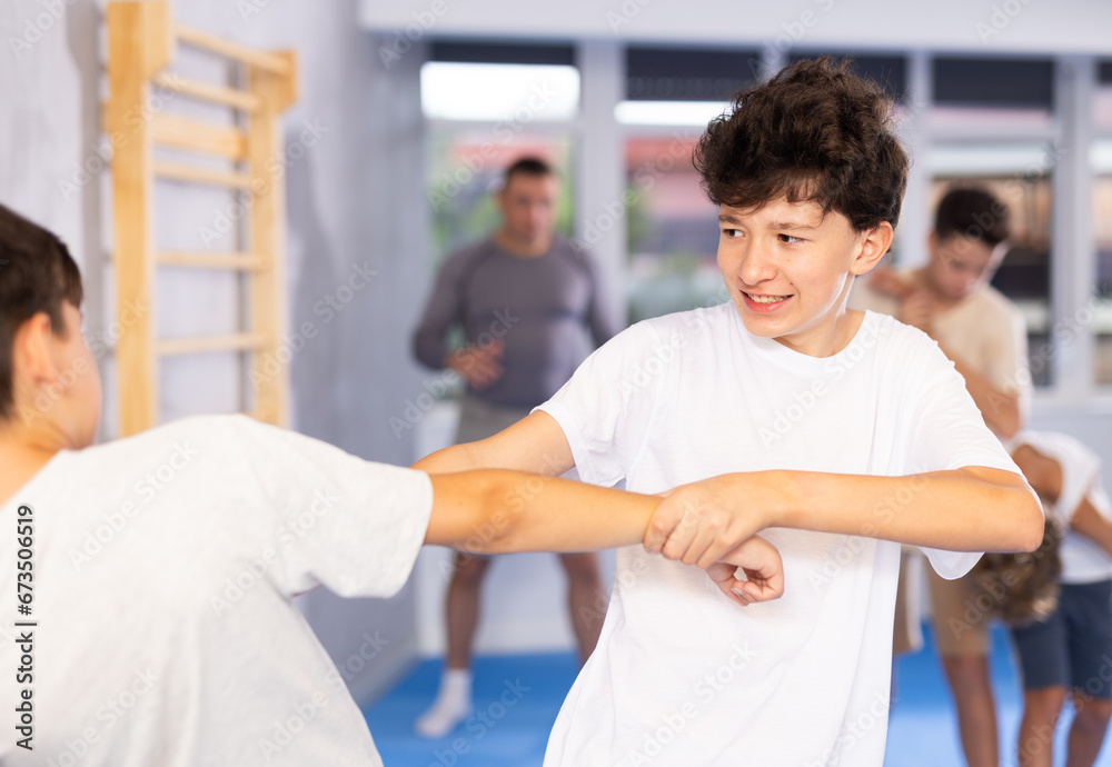 Focused teenage boys practicing close combat techniques in sparring in ...