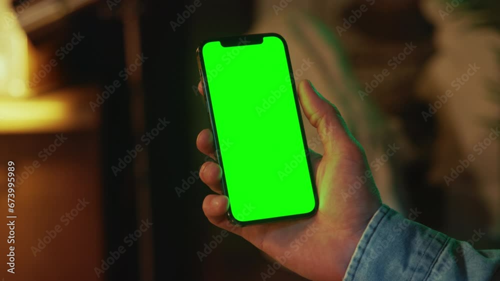 Phone with vertical green screen. Hands using typing on smartphone indoors. Social media. Mock ...