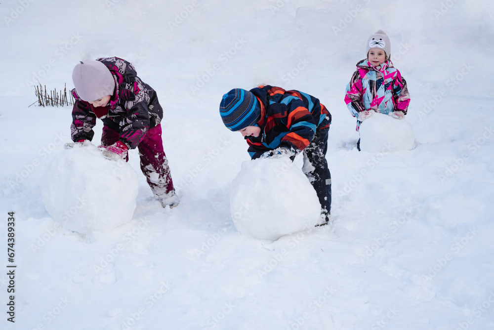 Happy children rolling a snow globe for a snowman. Children playing ...