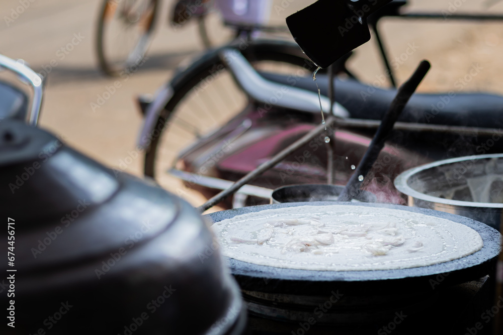 Dosa is being cooked on flat metal pan. It is a traditional South ...