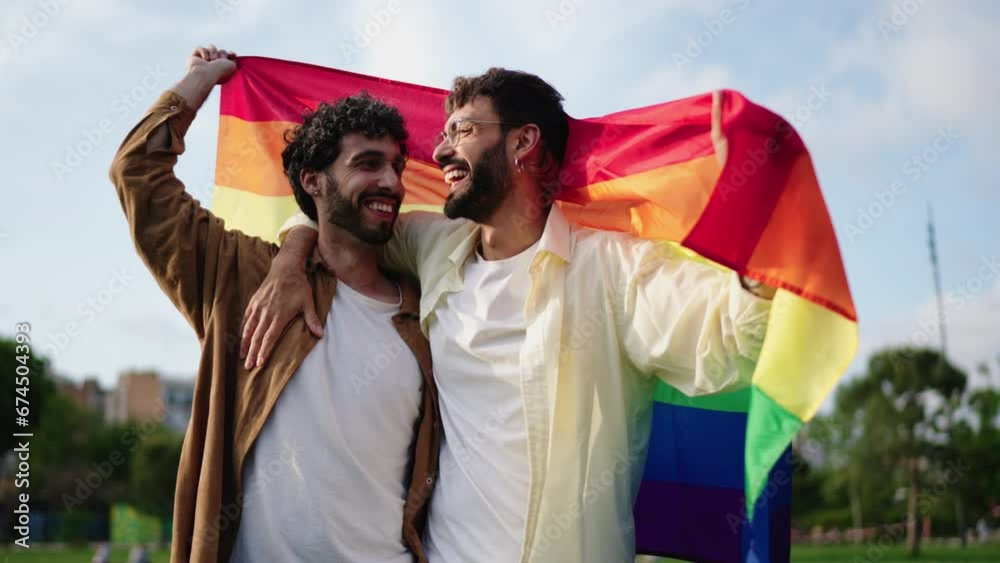 Cheerful gay couple celebrates love holding up rainbow pride flag ...