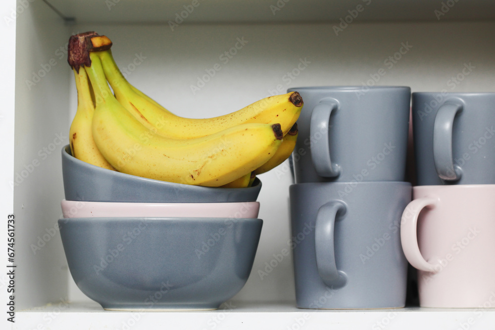 Bananas in kitchen cabinet. Coffee mugs. Tea cups. Milk soup bowls ...