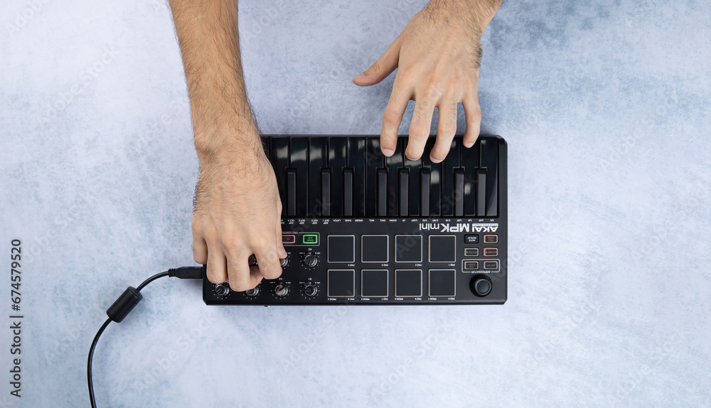 Male hands play the keys and rotate the encoder of the midi keyboard ...