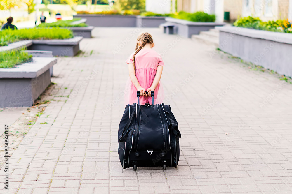Full length shot of a little girl walking and pulling a suitcase. Back ...
