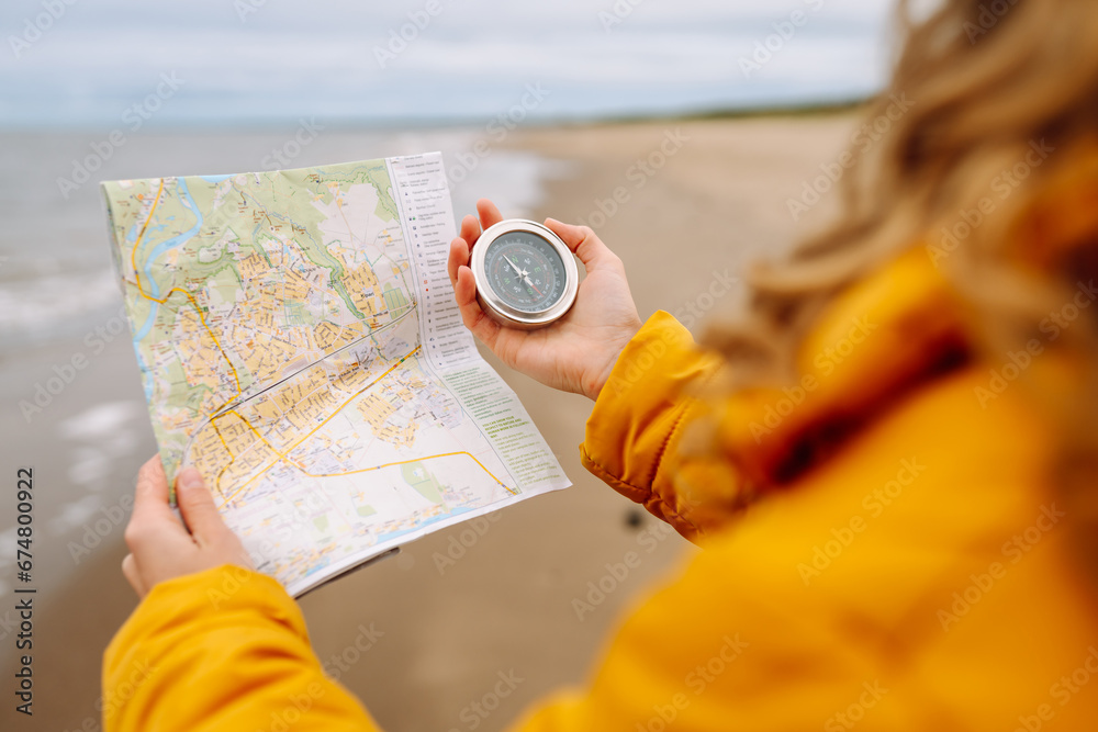 A young woman traveler with a compass and a map in her hands, reading a ...