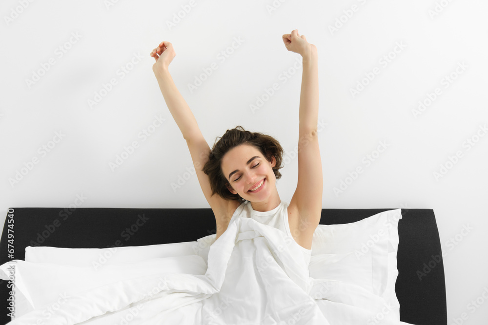 Beautiful young woman waking up in her bedroom, stretching hands with ...