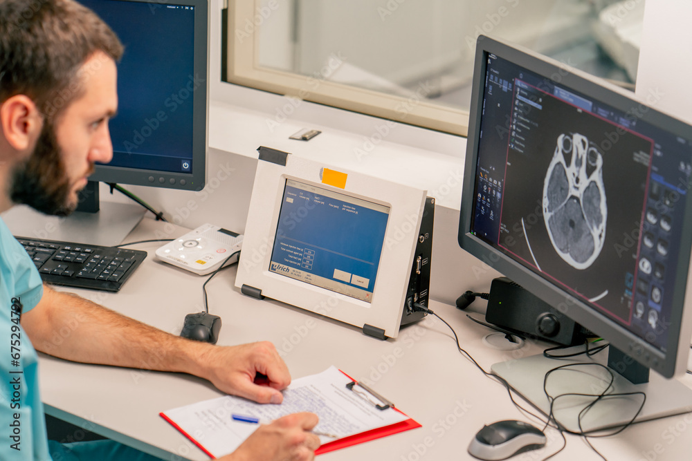 Concentrated male physician sits at a computer monitor in a room for ...