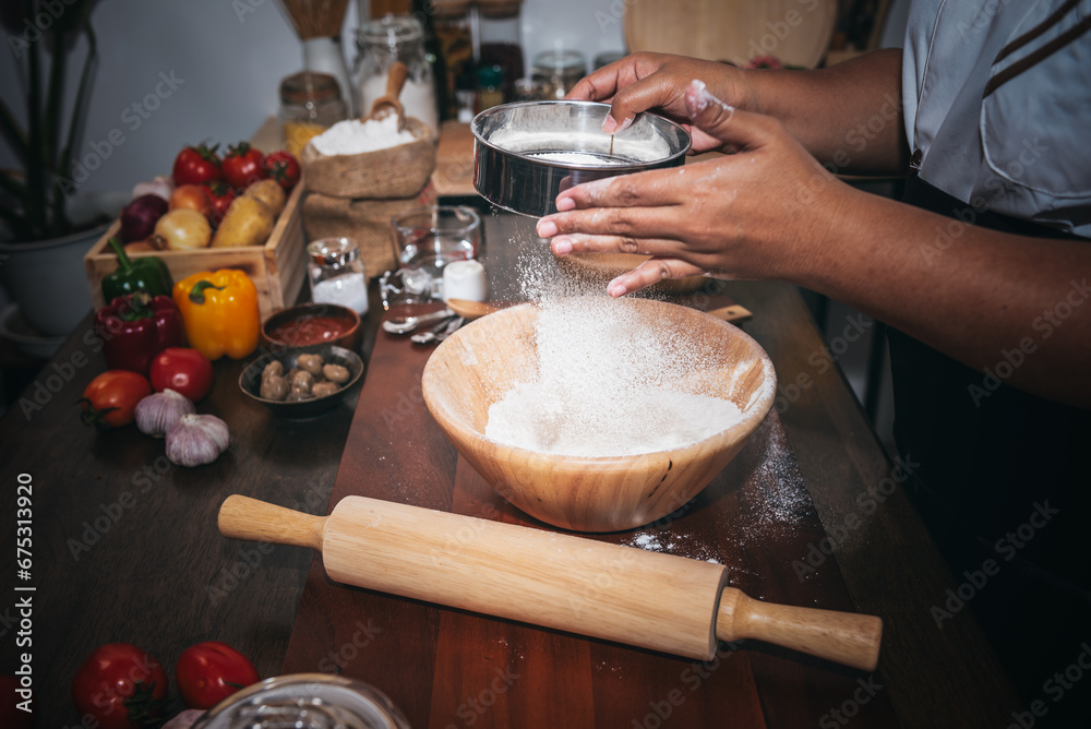 woman standing in the kitchen and using the sieve, sifting the flour ...