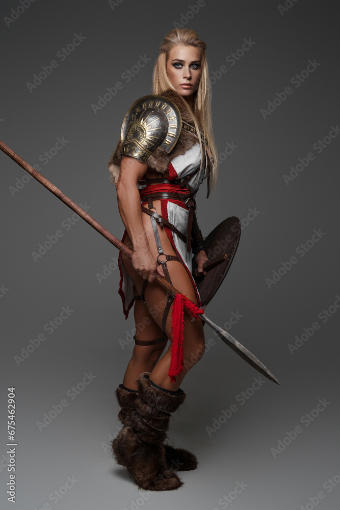 A muscular blonde Viking woman in fantasy armor, featuring a white mantle, leather straps ...