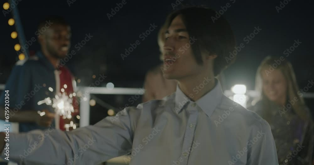 Joyful Asian guy dancing with burning bengal lights relaxing at rooftop ...
