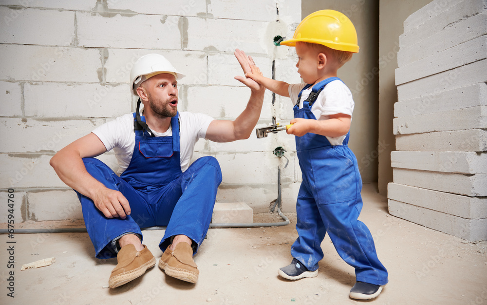 Male builder and little boy slapping hands giving high five in room ...