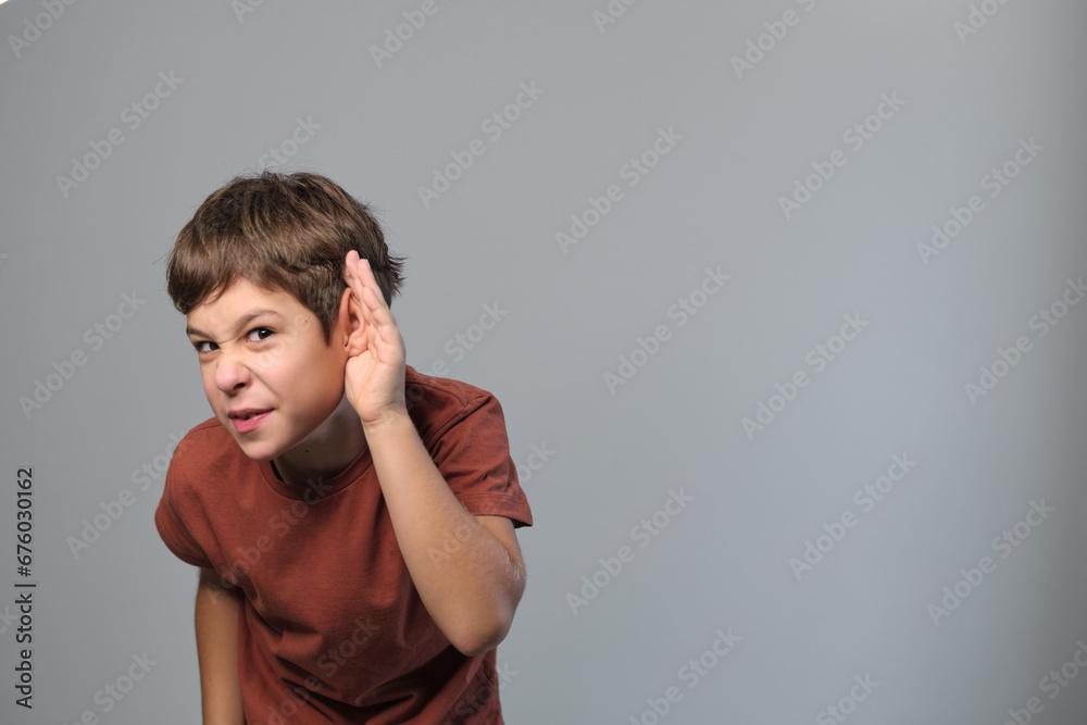 young boy with attentive expression holds his hand to his ear ...