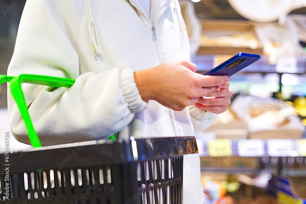 A young woman with a grocery cart is shopping in a supermarket, looking ...