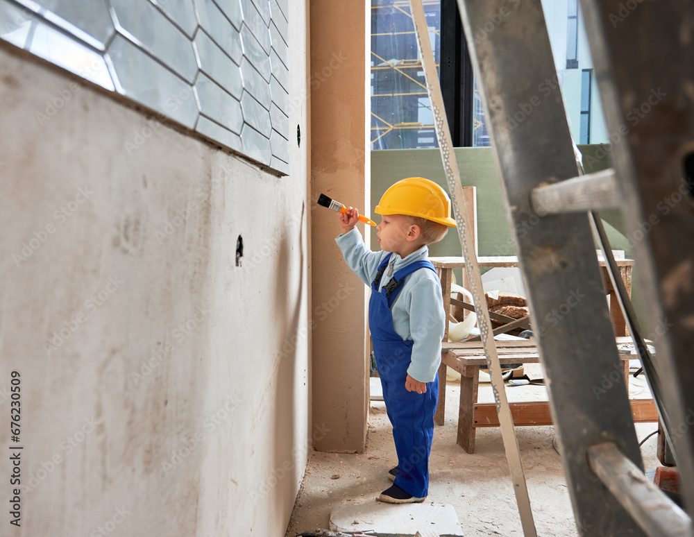 Side view of little boy construction worker painting wall with brush in ...