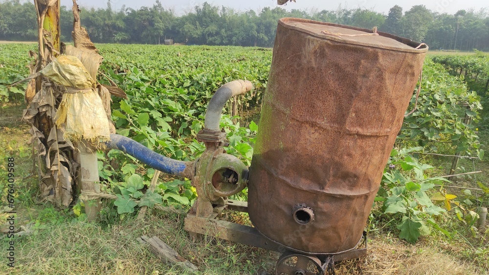 old rusty bucket. Farmer using water pump engine and blue pipe to pump ...