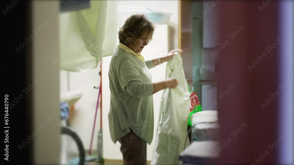 Candid scene of an older woman folding sheets in laundry room. Domestic ...