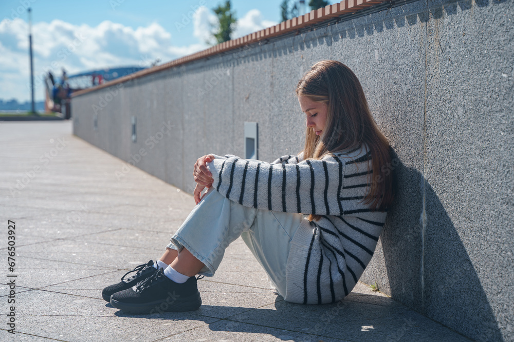 Sad teenage girl sitting alone on the asphalt in the city, teenage ...