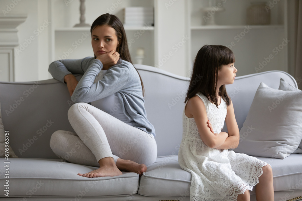 Unhappy young mother and stubborn little daughter with arms crossed ignoring each other after ...