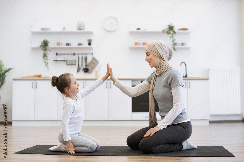 Muslim mother and little daughter engaged in fitness, yoga, exercise at ...