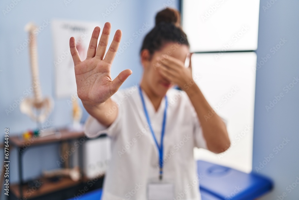 Young hispanic woman working at rehabilitation clinic covering eyes ...