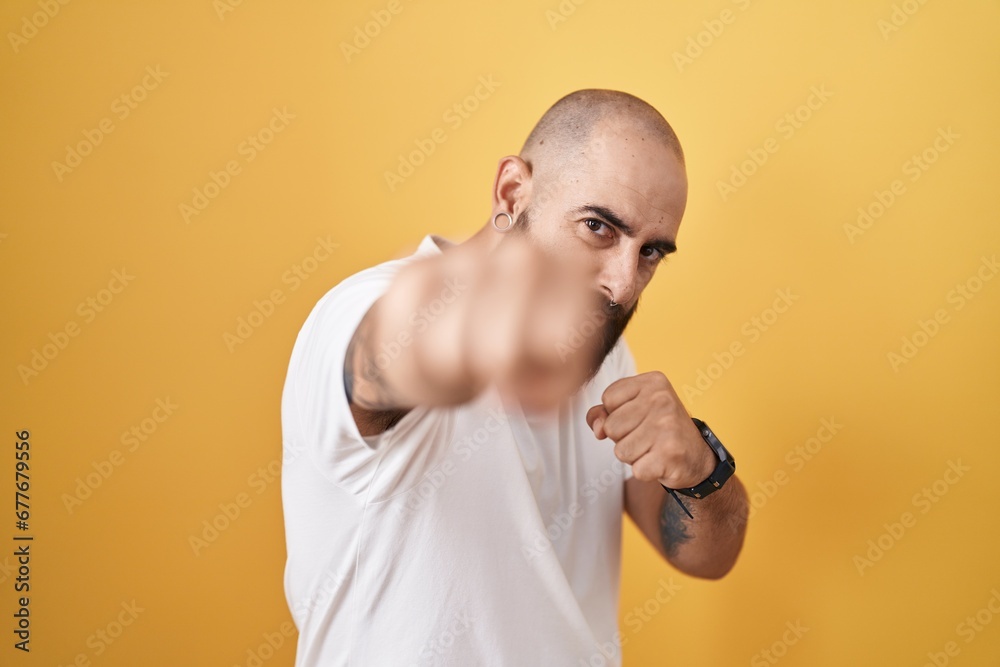 Young hispanic man with beard and tattoos standing over yellow ...