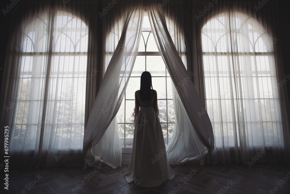 Bride near the window. the bride in a wedding dress opens the curtains ...