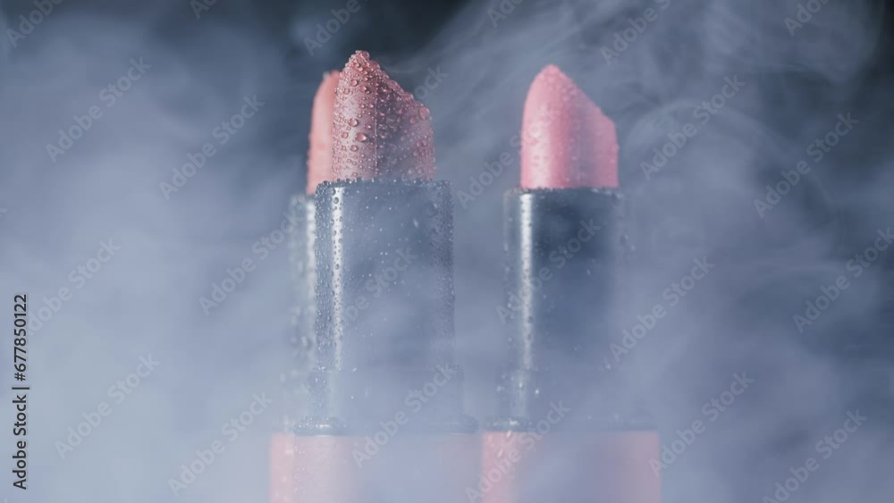 Red lipsticks make up close up black background with smoke and water ...